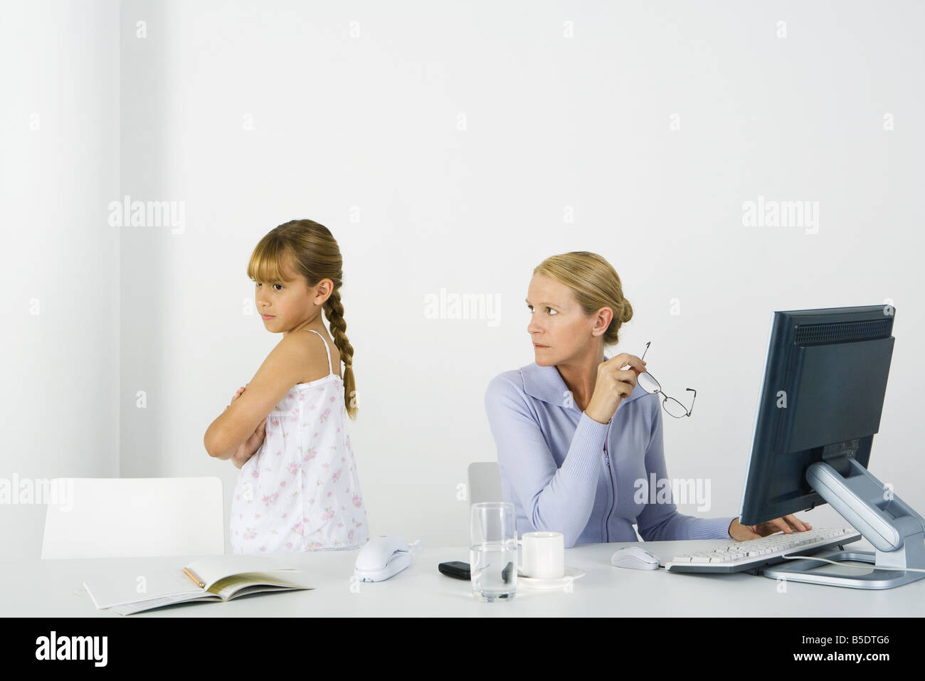 Woman sitting before computer, looking over shoulder at daughter ...
