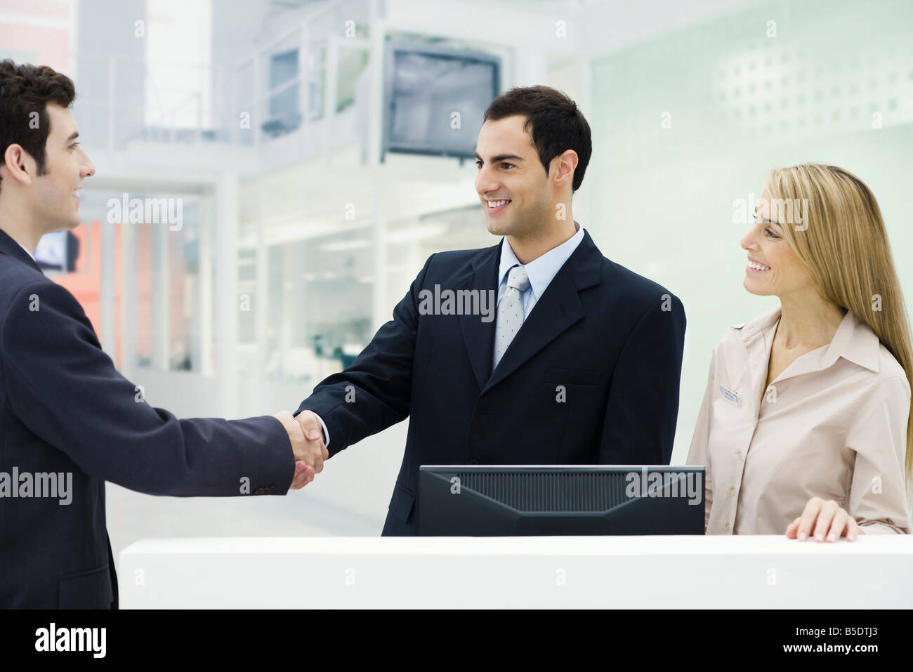 Three professionals standing at counter, men shaking hands Stock Photo ...