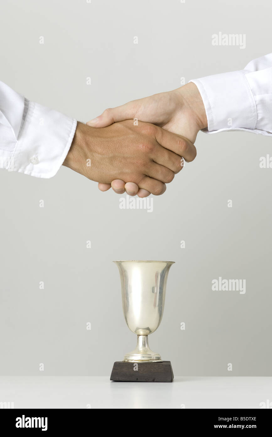 Shaking hands over trophy, cropped view Stock Photo - Alamy