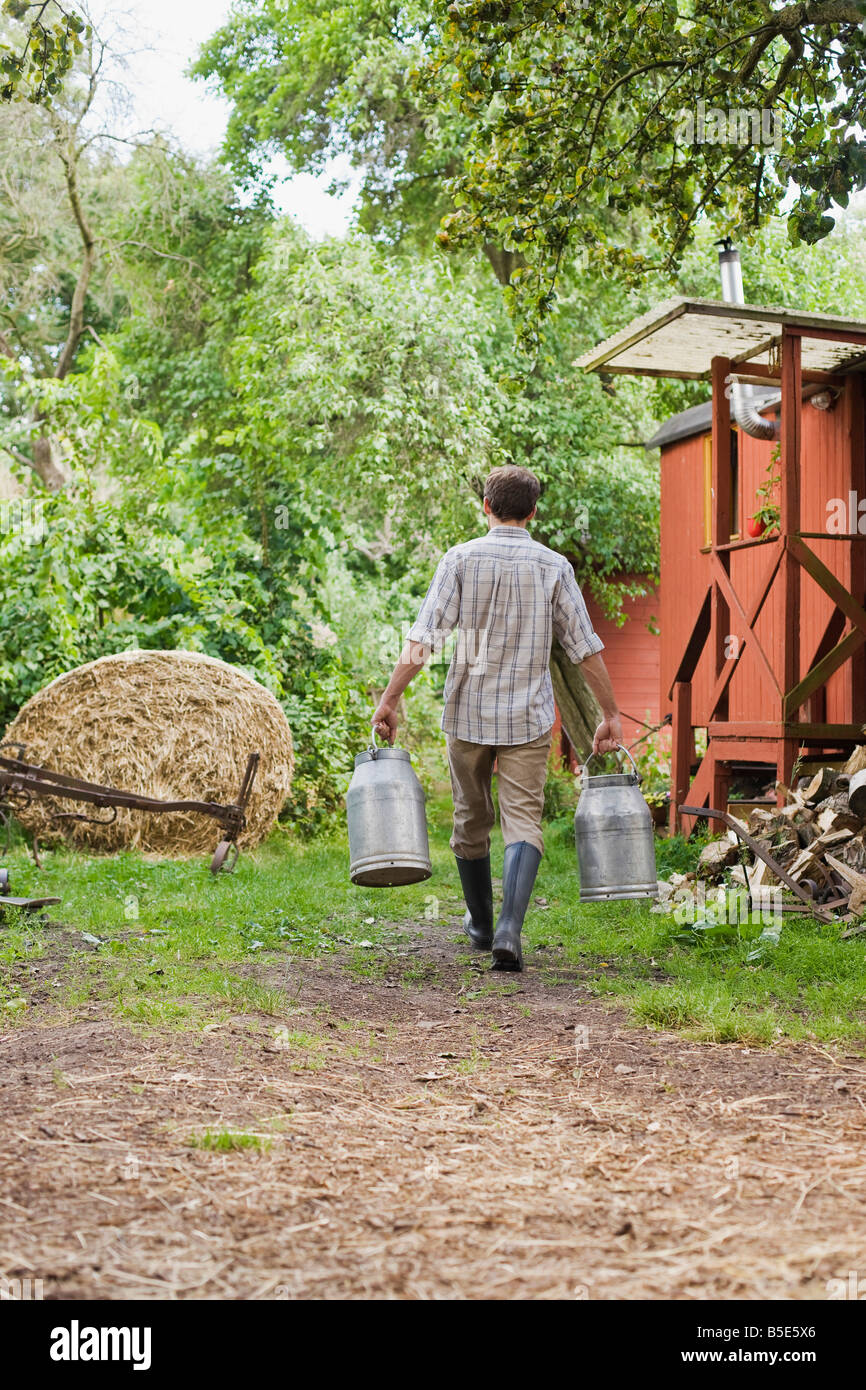 Farmer carrying milk cans, rear view Stock Photo - Alamy