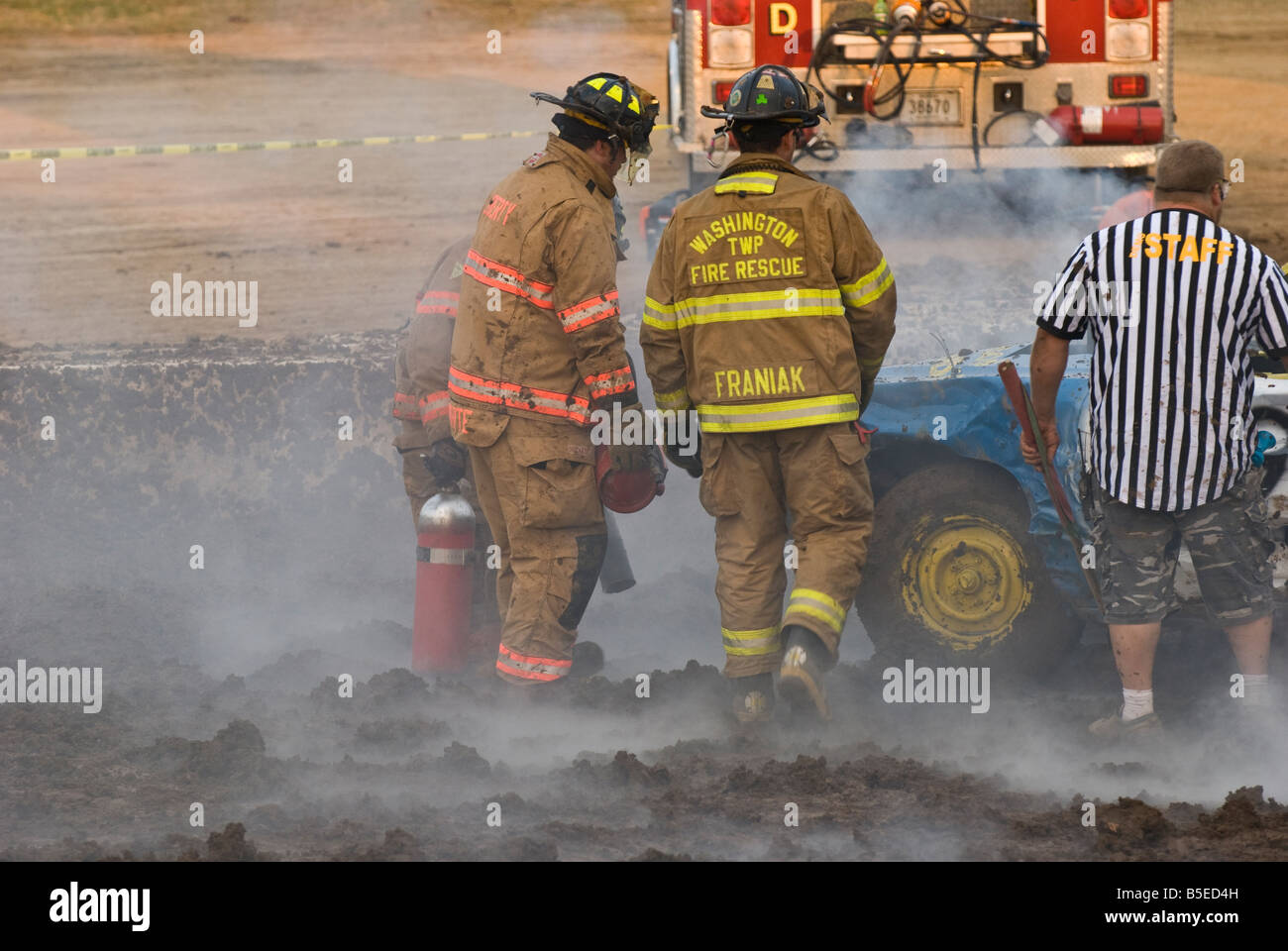 Fire fighter extinguishing fire on a car engine at a demolition derby ...