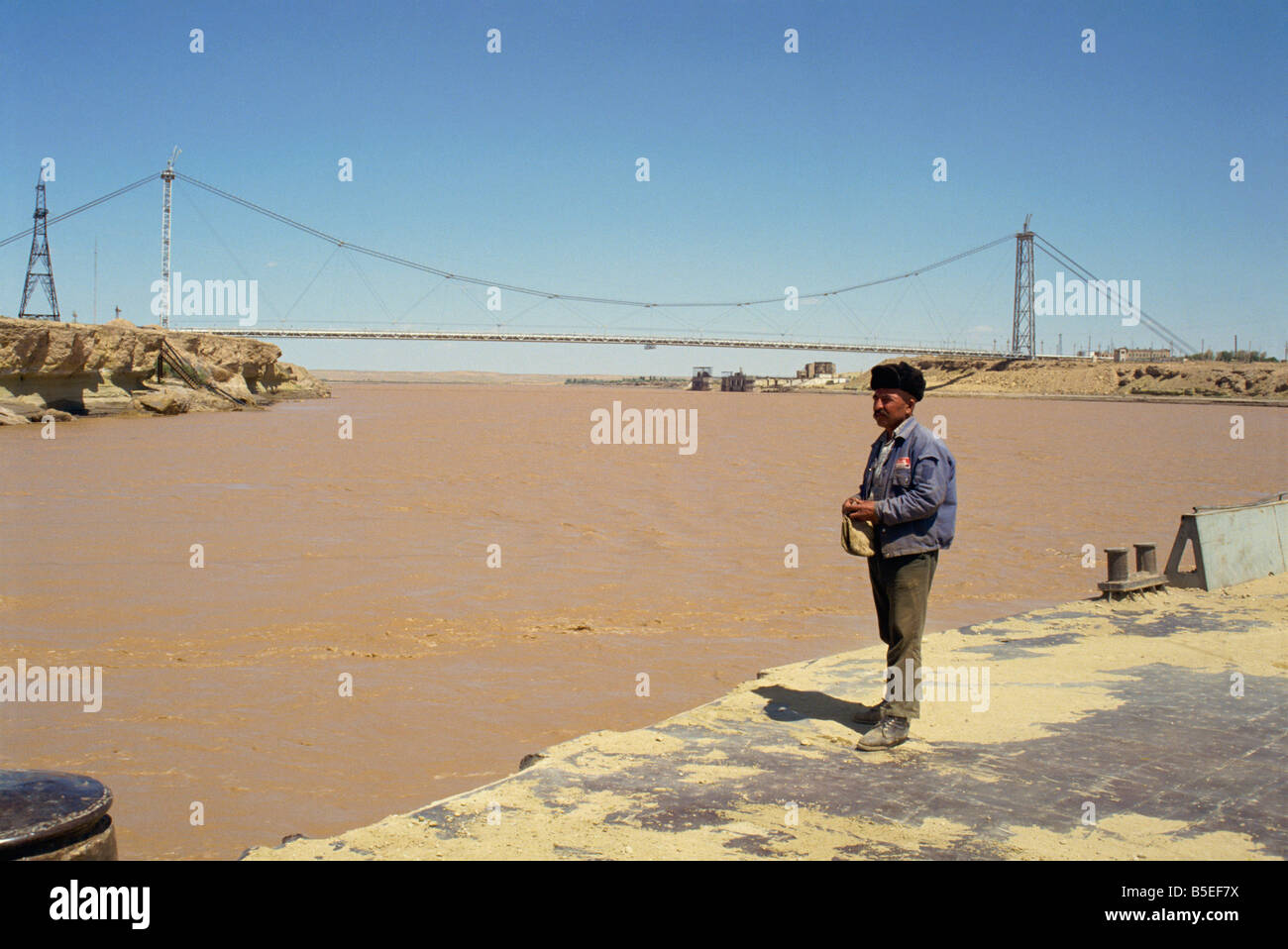 Man standing on the river bank in front of a bridge over the River Oxus ...