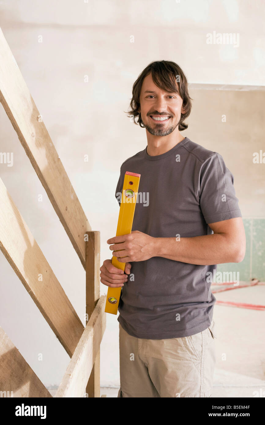 Young man holding spirit level, smiling, portrait Stock Photo - Alamy