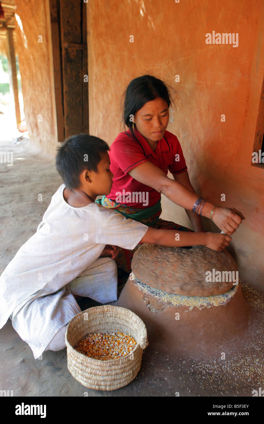Nepal: mother and son grinding rice with a stone grinder in a village ...