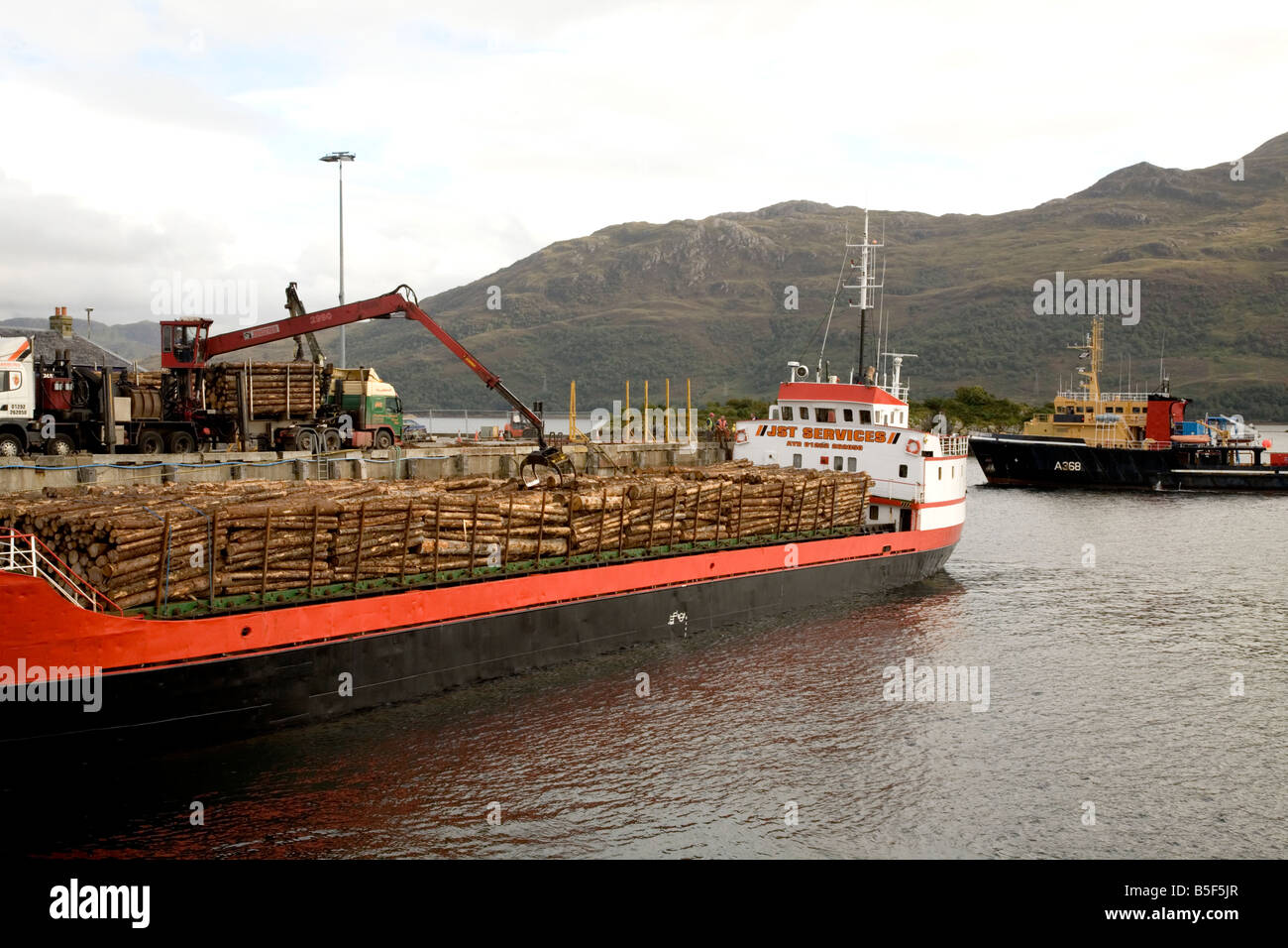 A freight boat being loaded with logs by crane at the quayside in Kyle ...