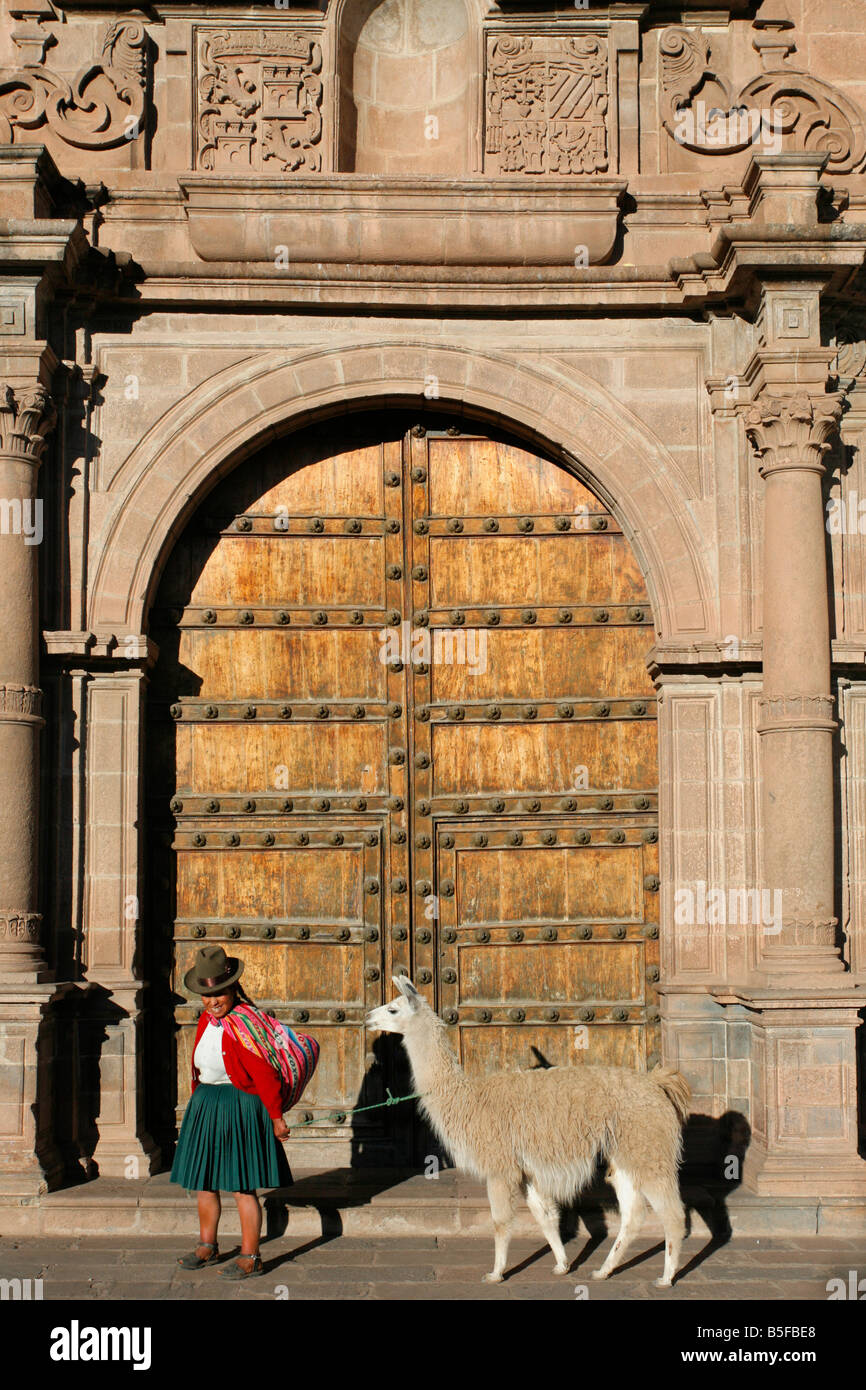Quechua woman in traditional dress with a llama walking past a church ...