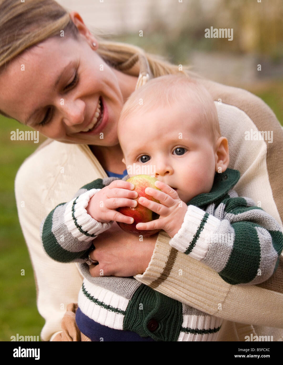 A young mother smiles while holding her baby boy, who is clutching an ...
