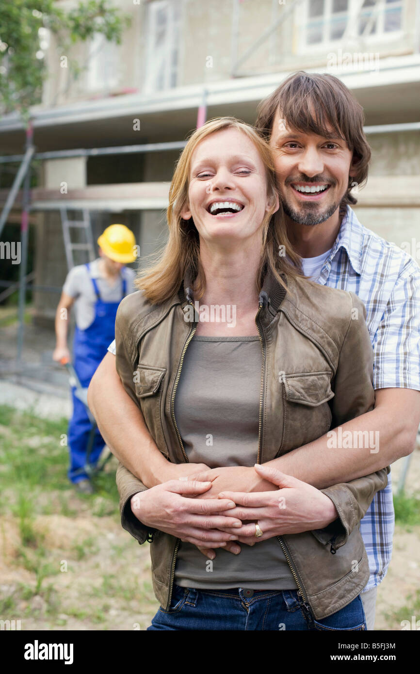 Young couple at site embracing, construction worker in background Stock ...