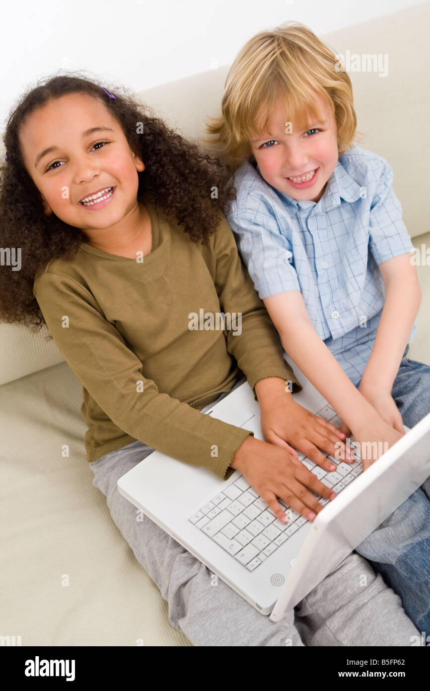 Two young children having fun on a laptop while sitting on a settee ...