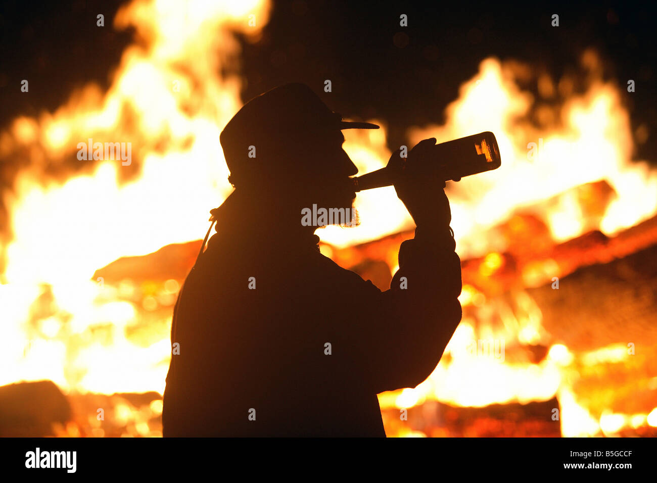 Silhouette of a man with a cowboy hat drinking beer near a bonfire ...