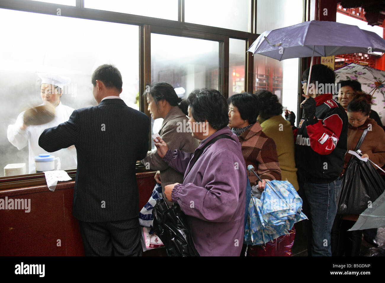 Pedestrians watching a cook trough a restaurant window, Shanghai, China ...