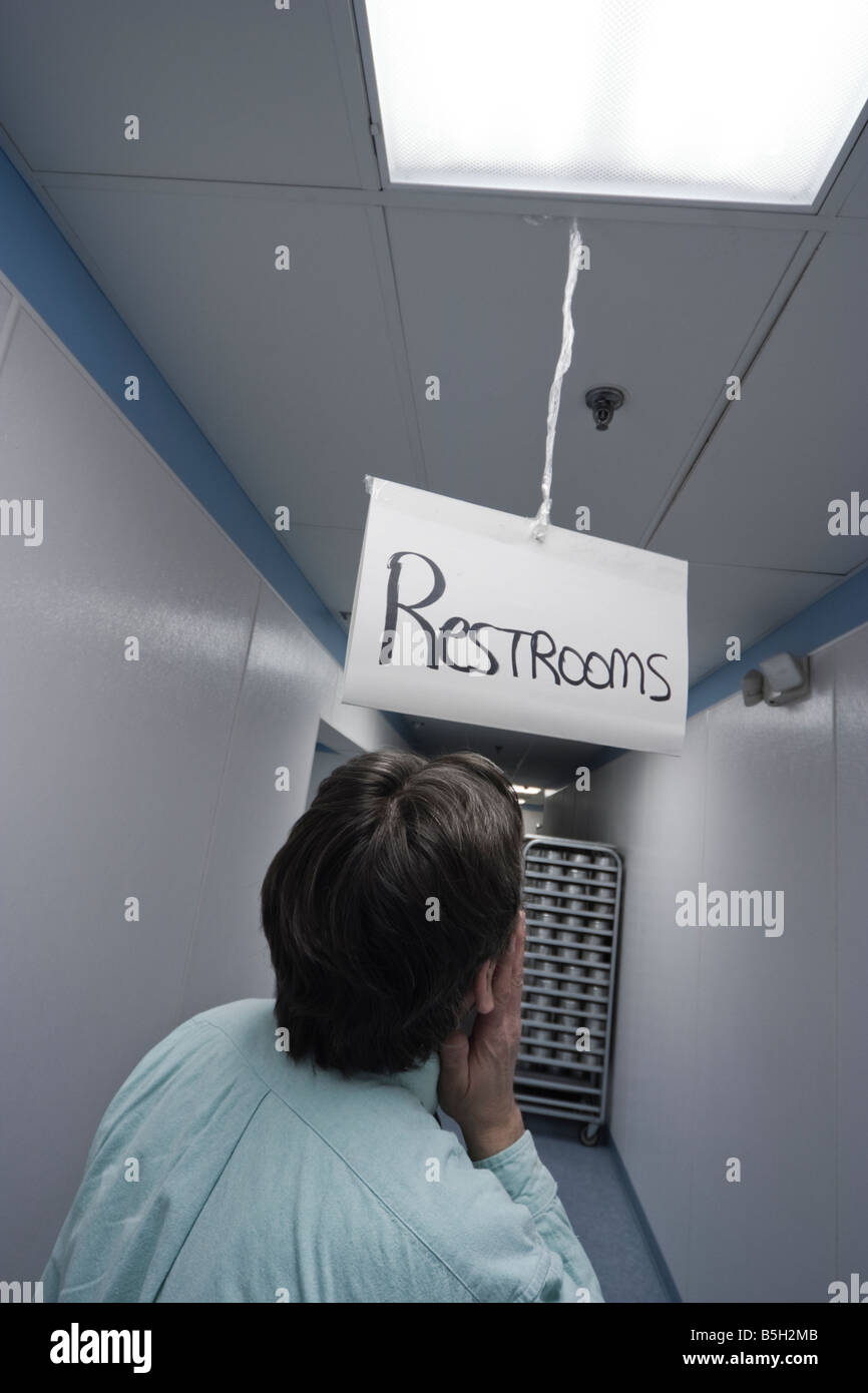 Man looking at a hanging sign in a factory that reads Restrooms MODEL ...