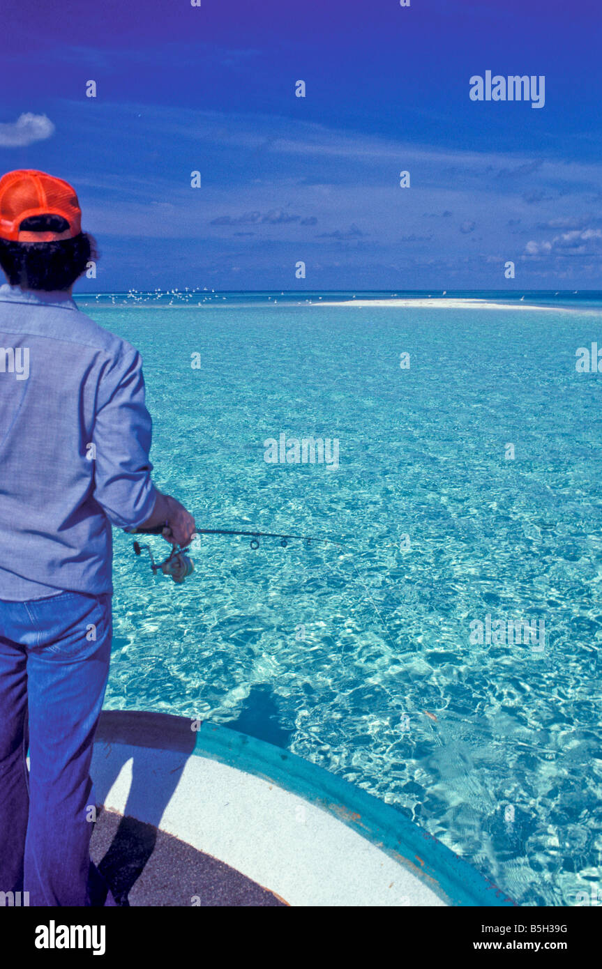 Tropical saltwater fishing bonefishing angler stands at boat bow over ...