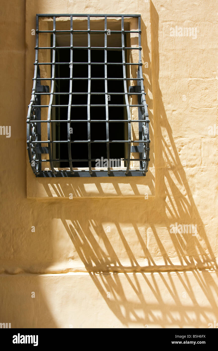 An open window with an iron grill over it, casting a long shadow on a ...