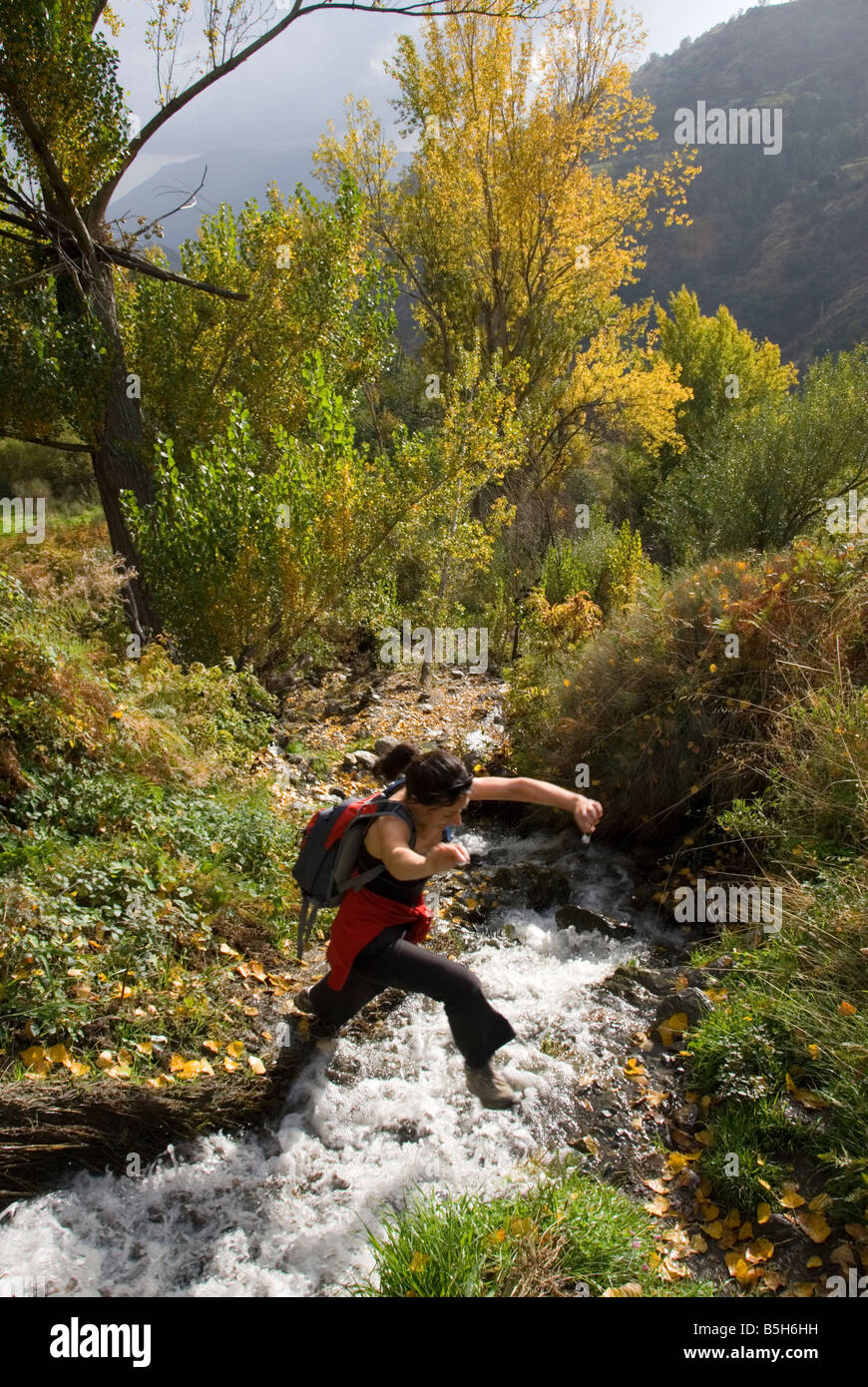 Woman jumping a stream on a hiking trail in the Poqueira valley Sierra ...
