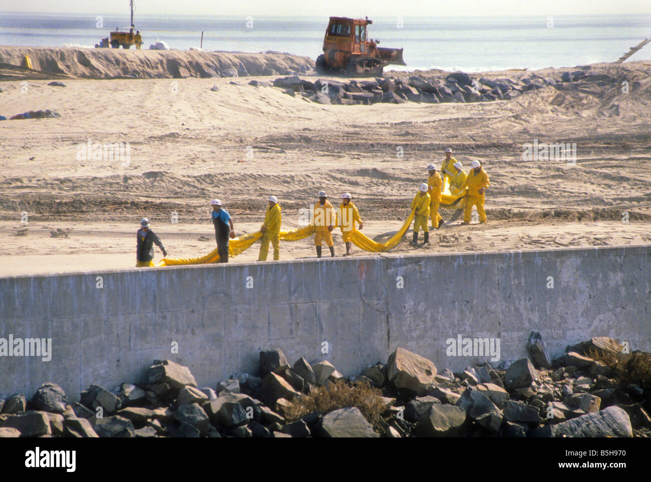 Workers carry a long flexible dam to control an oil spill in California ...