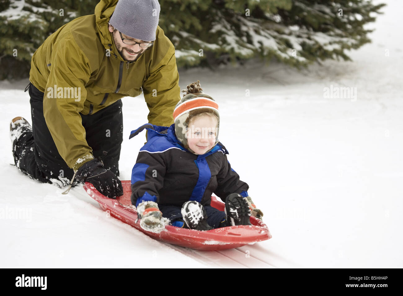 A toddler boy and his father ride a red sled during snow play Stock ...