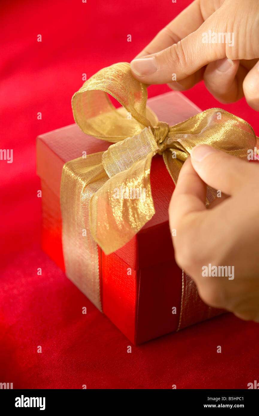 red gift box with woman's hand tying a metallic gold ribbon Stock Photo ...