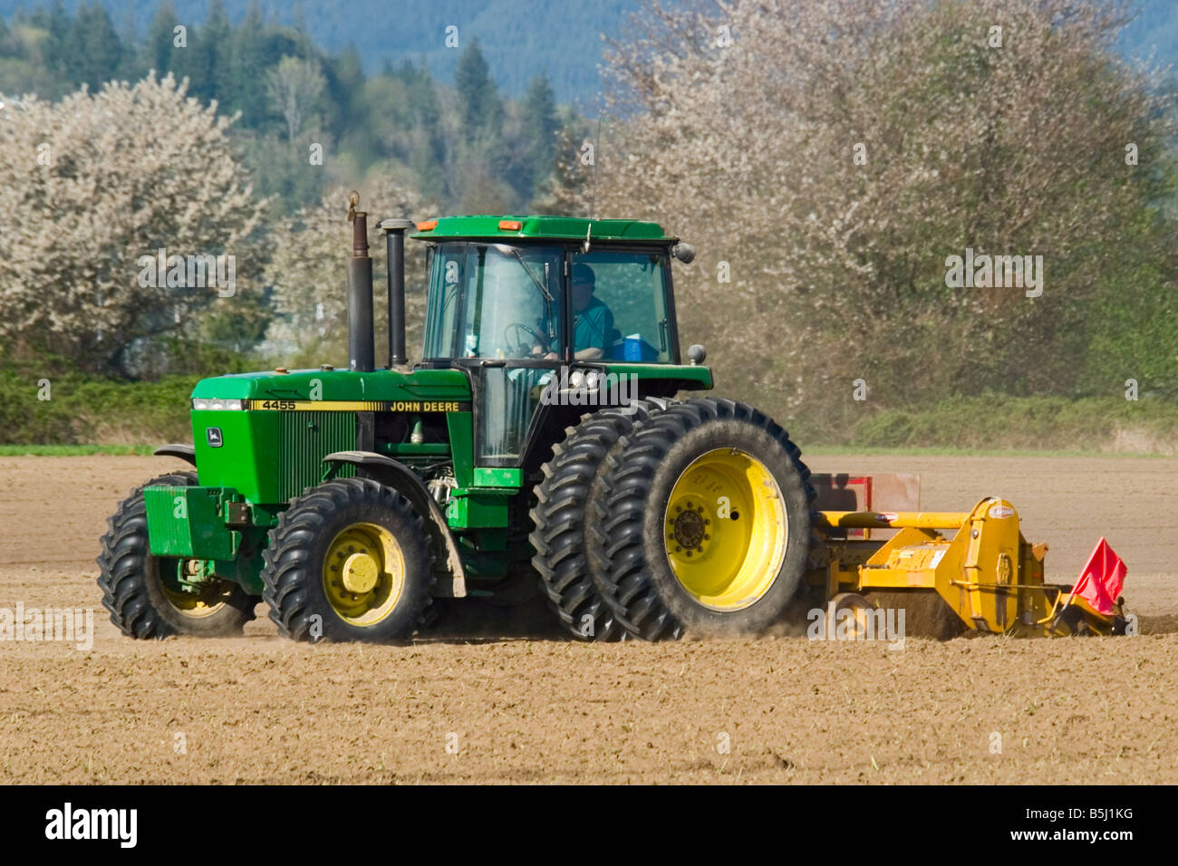 A tractor pulling a roto-tiller works to prepare a seed bed to plant ...