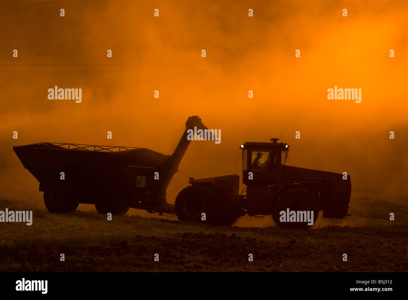 A tractor pulling a grain cart at sunset in very dusty conditions in ...