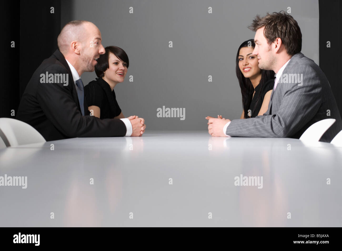four business people sitting around conference table Stock Photo - Alamy