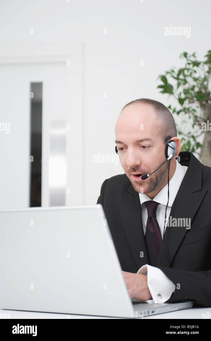 portrait of businessman wearing headset working with laptop computer ...