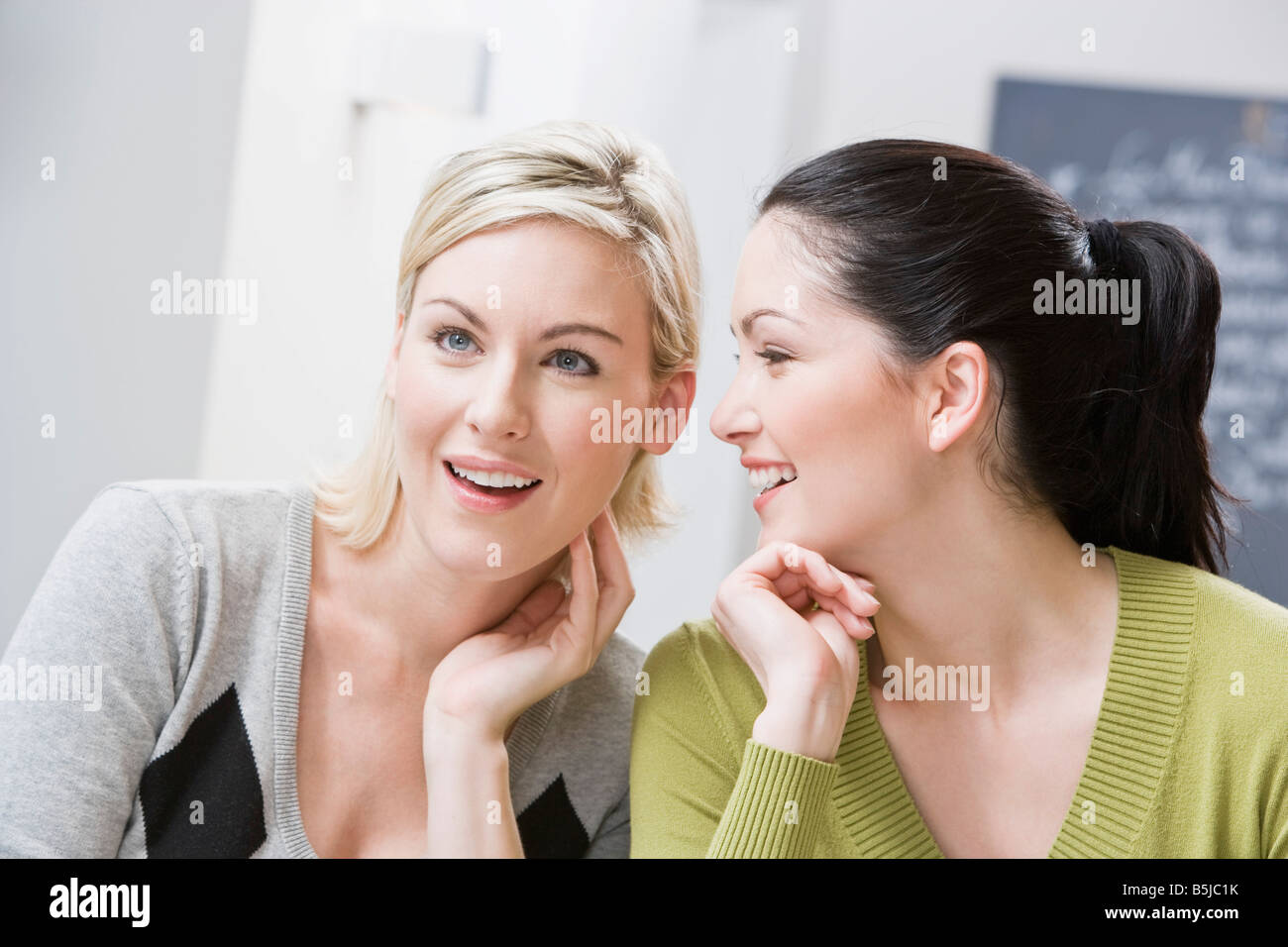 two female friends at restaurant whispering to each other Stock Photo ...