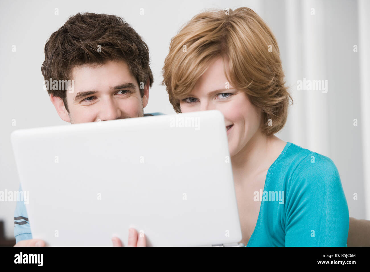 young couple hiding behind laptop computer Stock Photo - Alamy