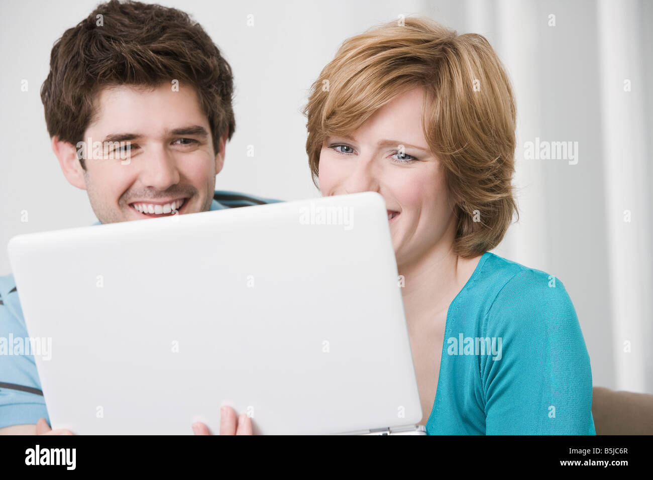 young couple hiding behind laptop computer Stock Photo - Alamy