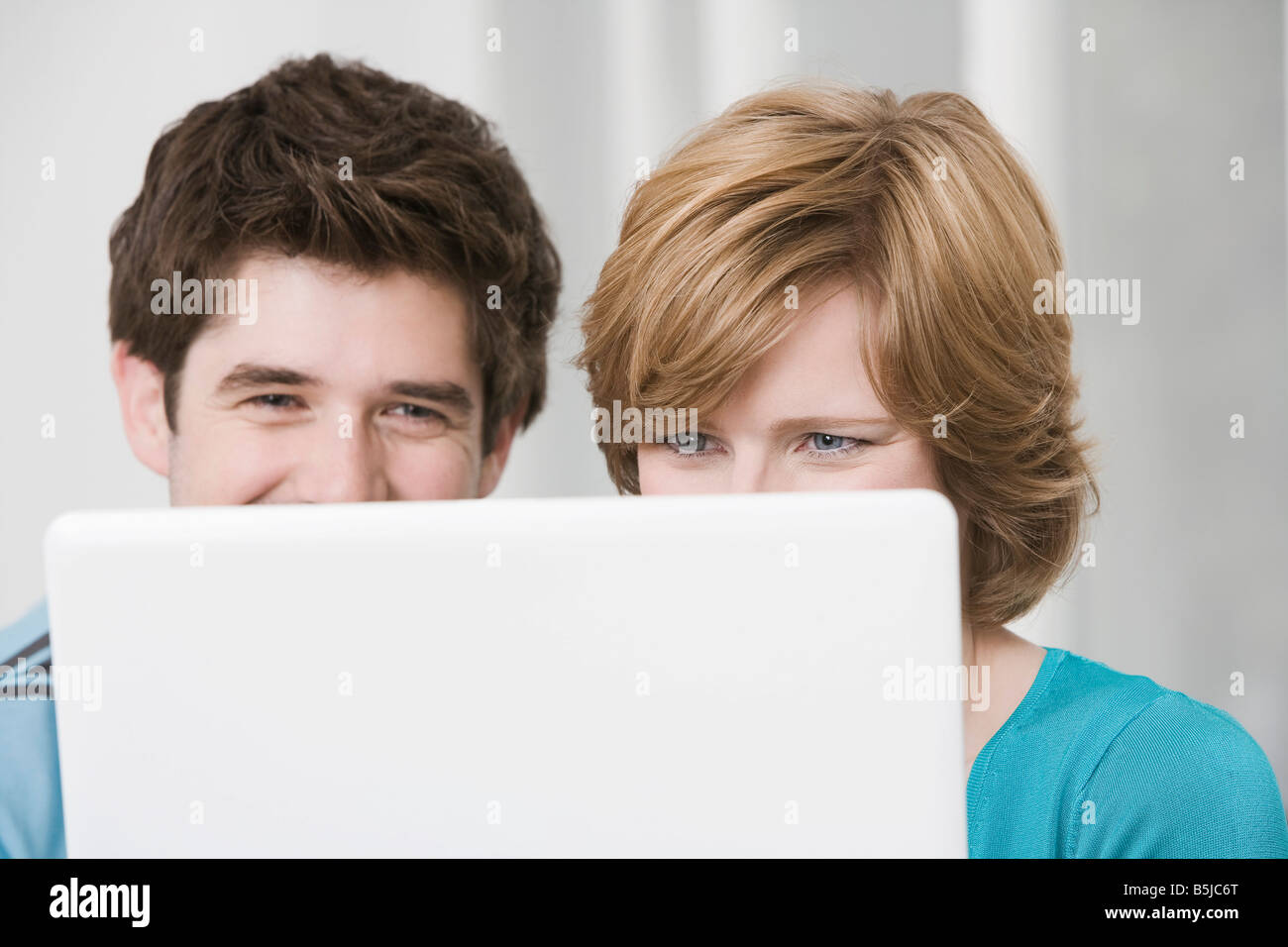young couple hiding behind laptop computer Stock Photo - Alamy
