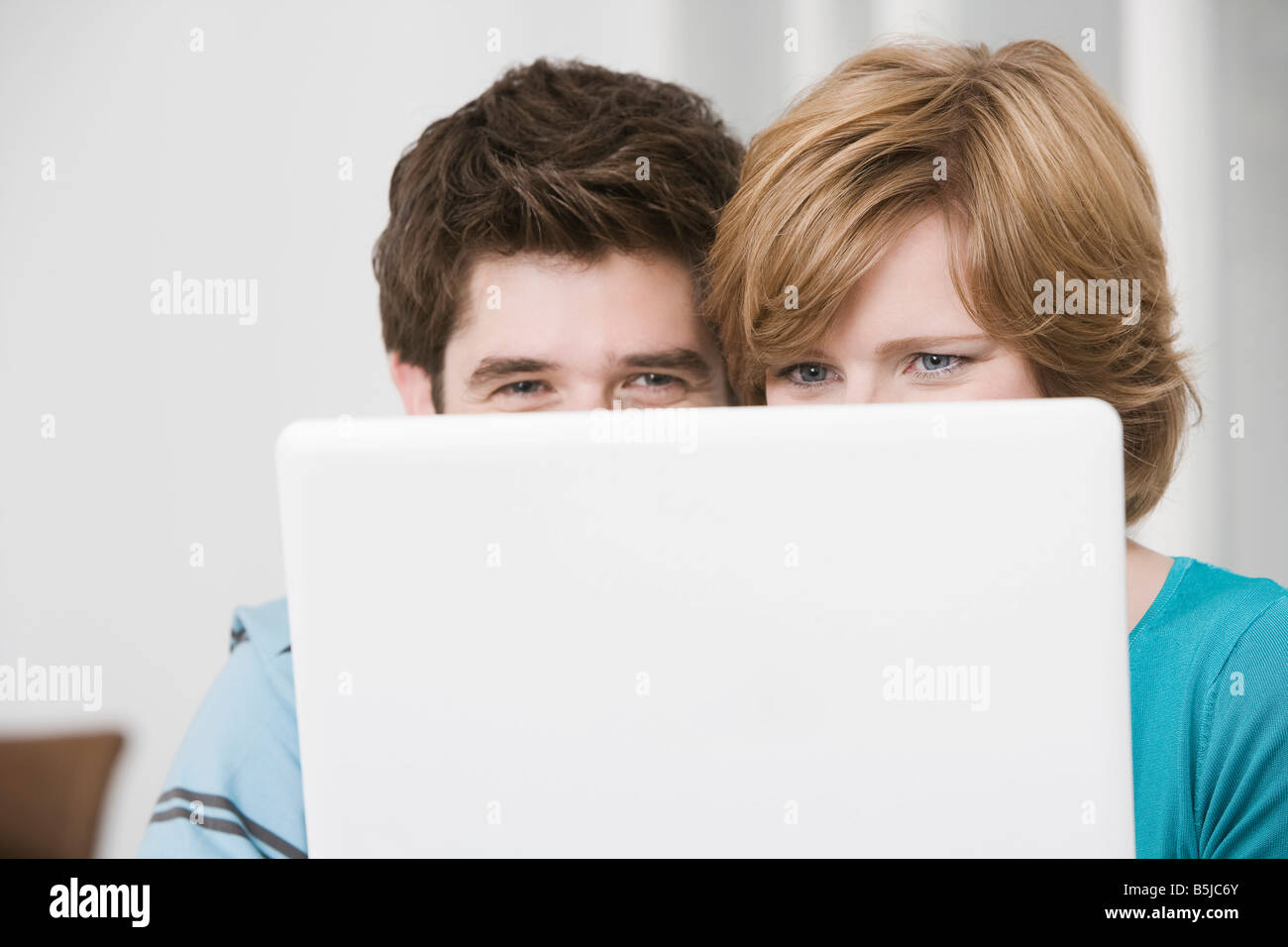 young couple hiding behind laptop computer Stock Photo - Alamy
