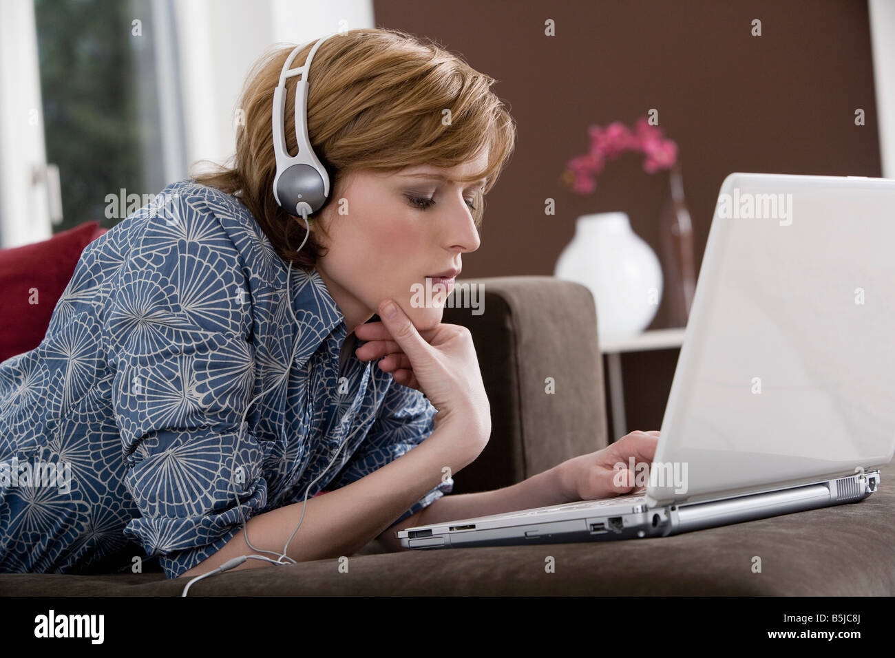 young woman at home wearing headset while working with laptop computer ...