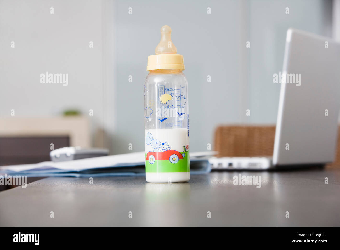 still life of baby bottle on table with laptop computer in background ...