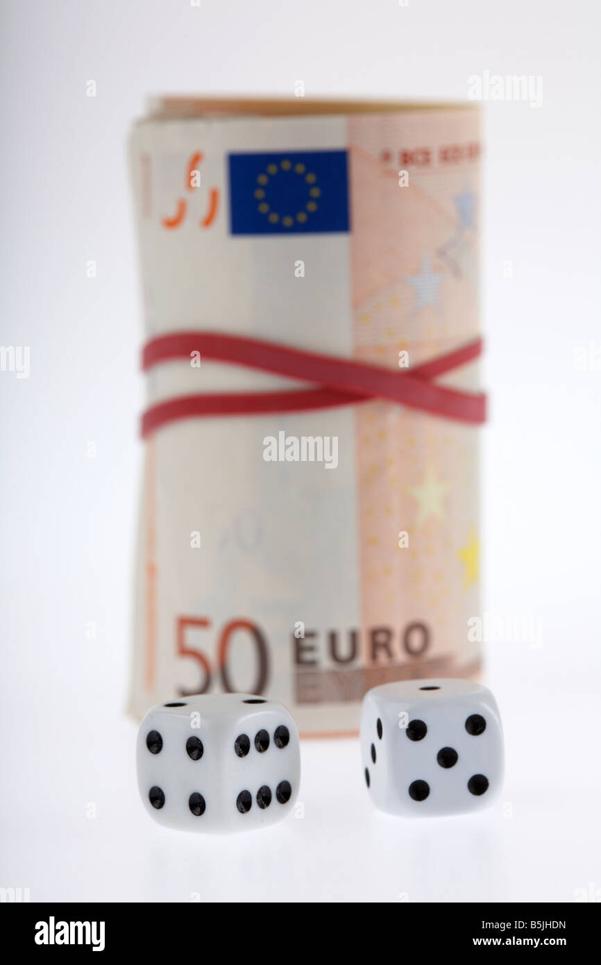 two dice in front of wad of 50 euro bank notes cash tied up in a roll ...