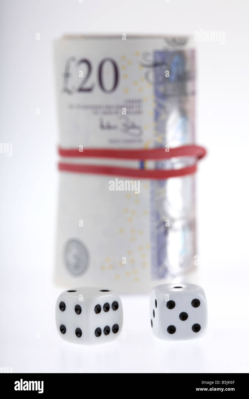two dice in front of wad of 20 pounds sterling bank notes cash tied up ...
