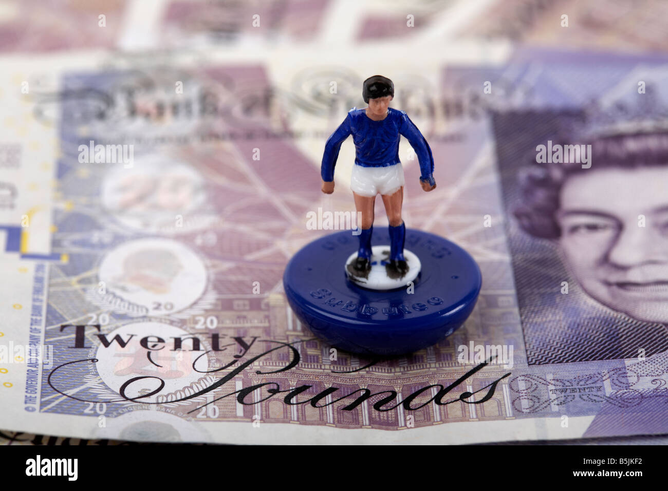 pile of 20 pounds sterling bank notes cash beneath toy footballer Stock ...