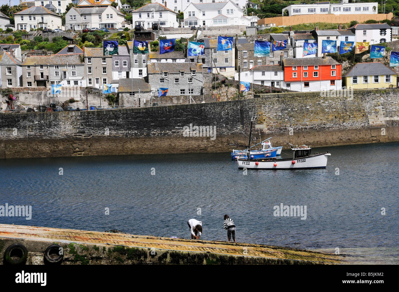 Two girls fish for crabs on the harbourside in Mevagissey Cornwall on a ...