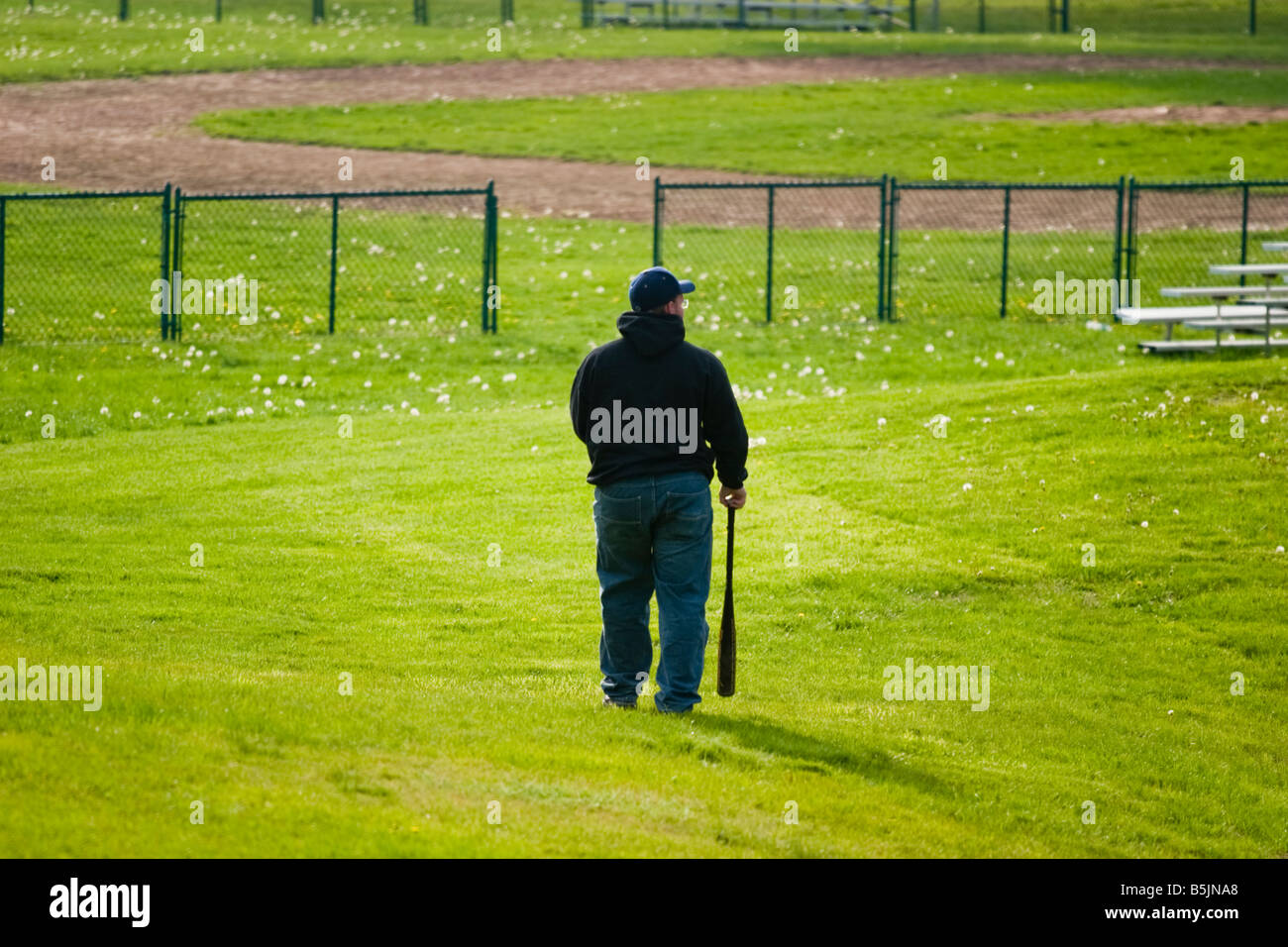 Young man carrying a bat walking towards the baseball field at a park ...