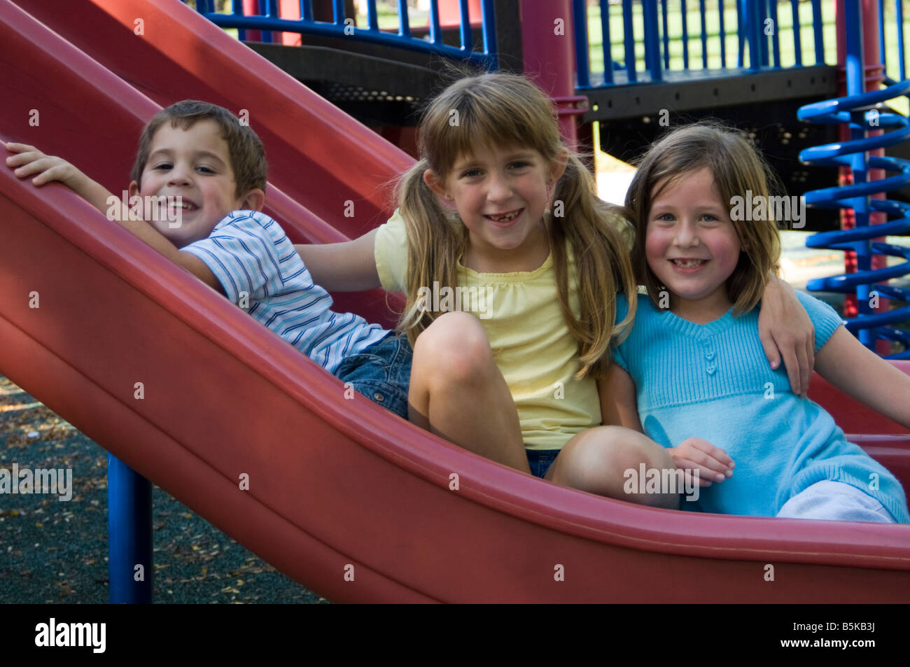 Three children, two girls and a boy, posed at the bottom of a slide ...