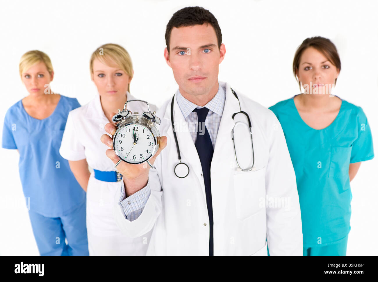 A male doctor backed by his medical team holding out an alarm clock ...