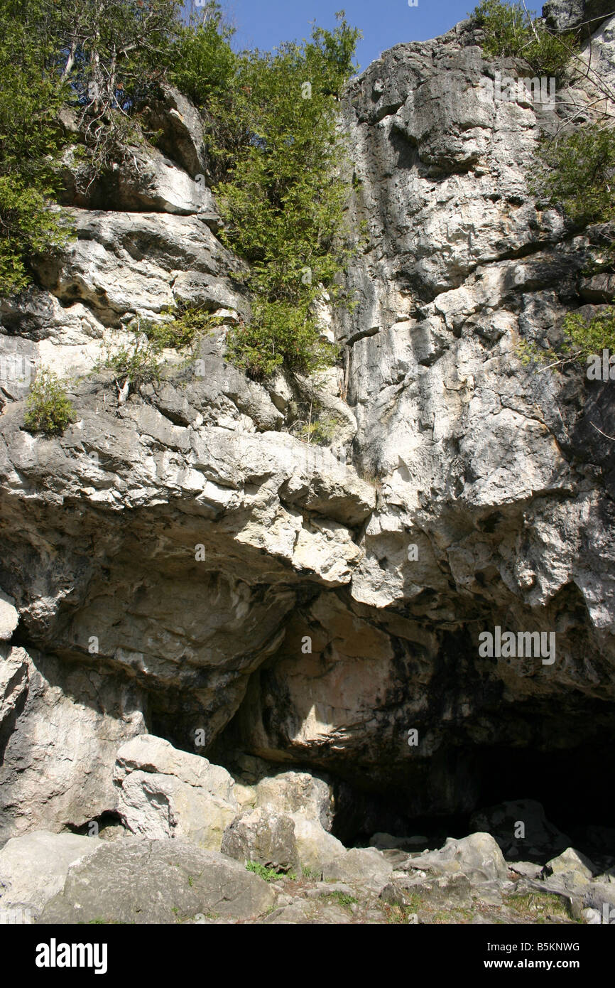 A limestone cave mouth, midway up a cliff, about ten feet above ground ...