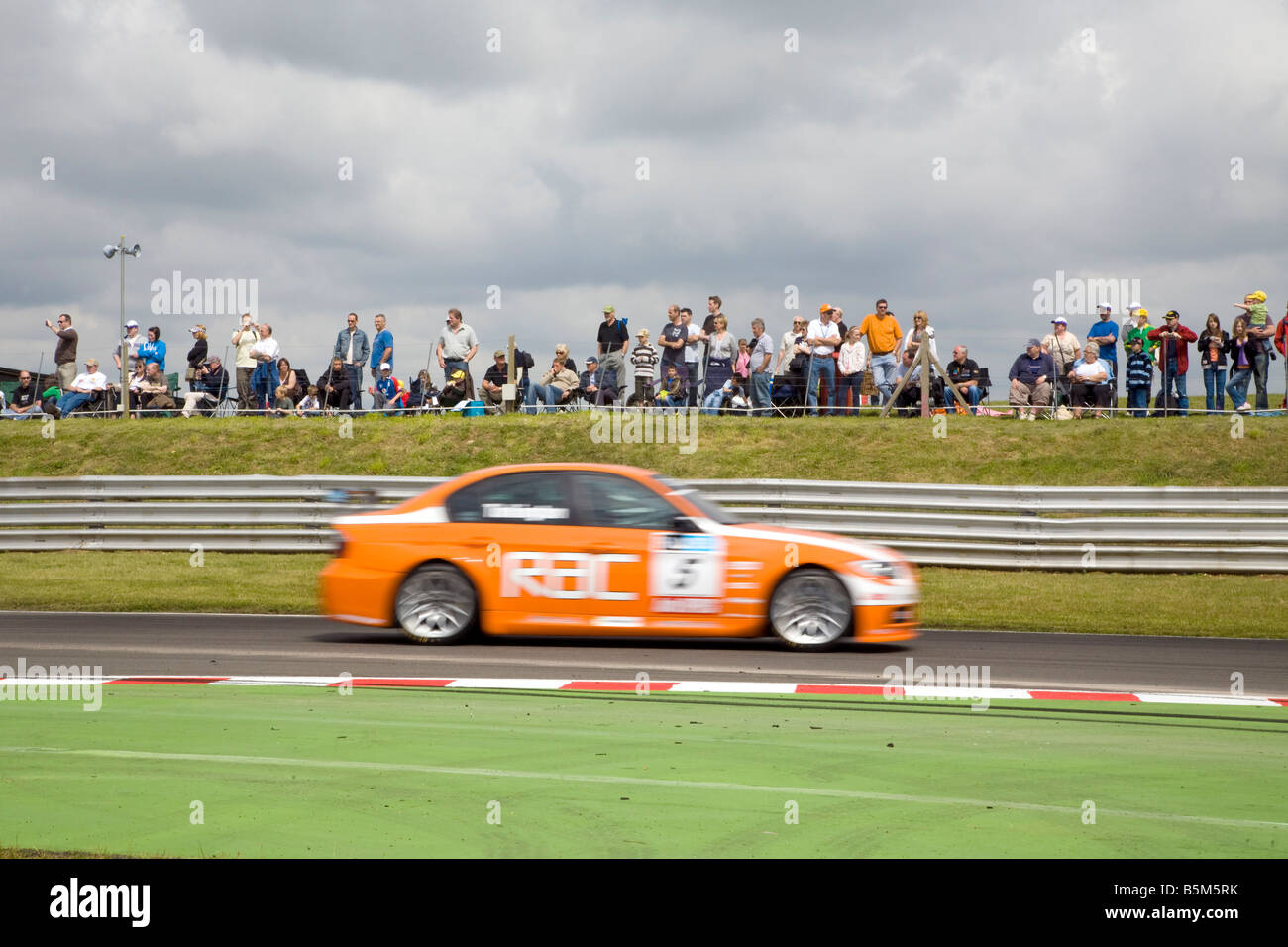 BLURRED ORANGE TEAM RAC CAR SPEEDS PAST SPECTATORS AT THE HiQ MSA ...