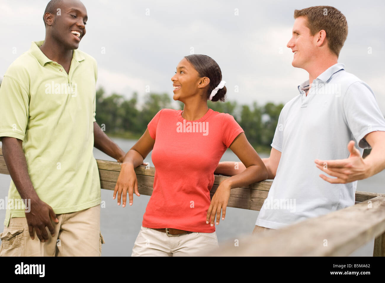 Three young people, two men and one woman, hang out at a dock in ...