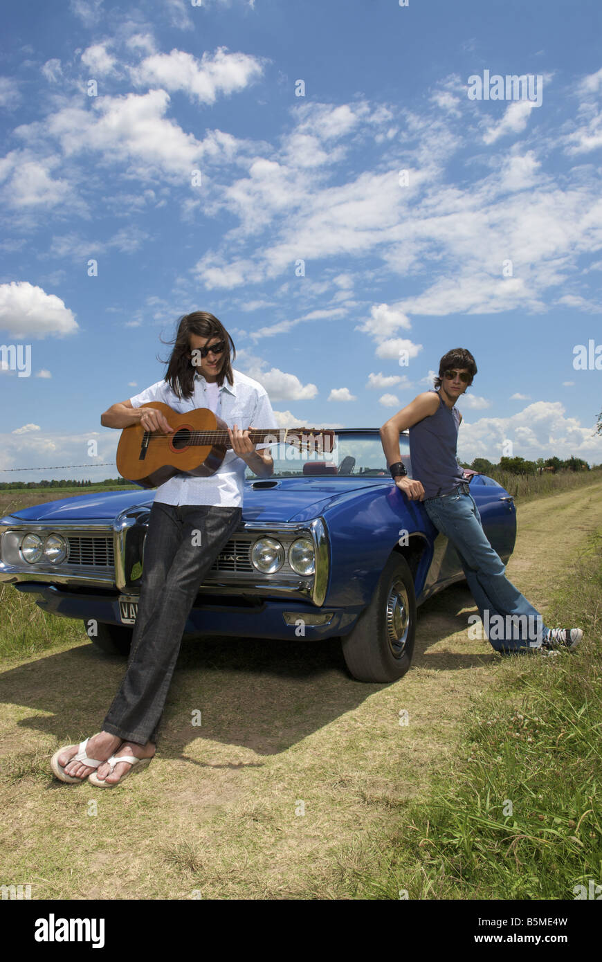 Two males leaning against a car and playing guitar Stock Photo - Alamy
