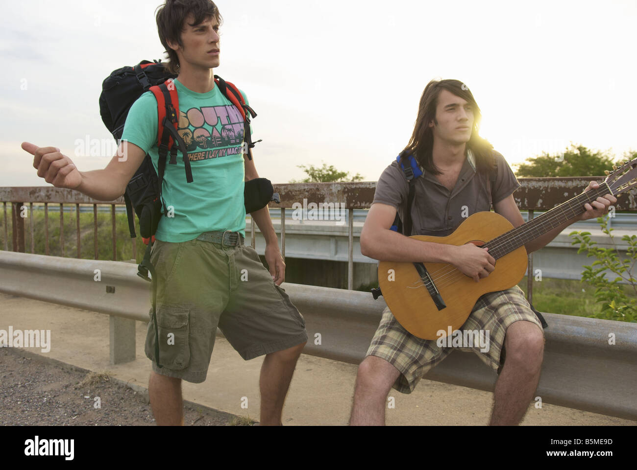 Two male backpackers hitch hiking with a guitar Stock Photo - Alamy