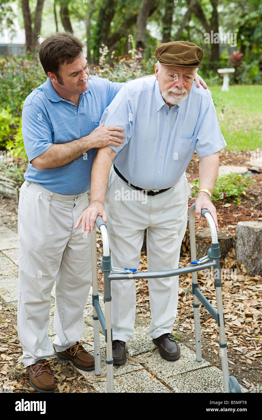 Senior man looks sad as he struggles to walk using a walker His adult ...