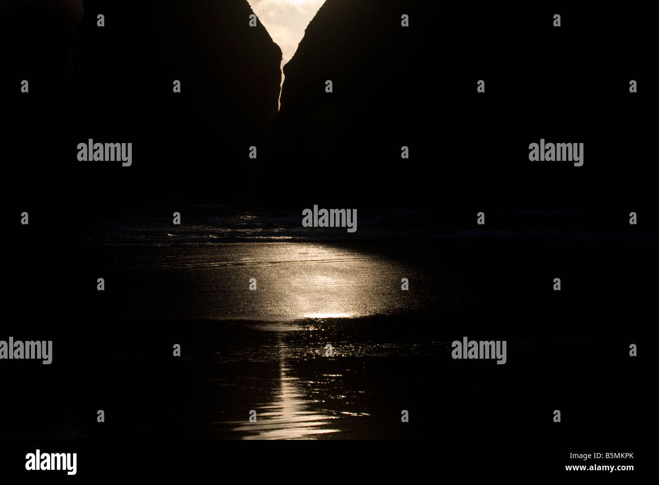 Sunset light filters through a slit between two sea stacks and ...