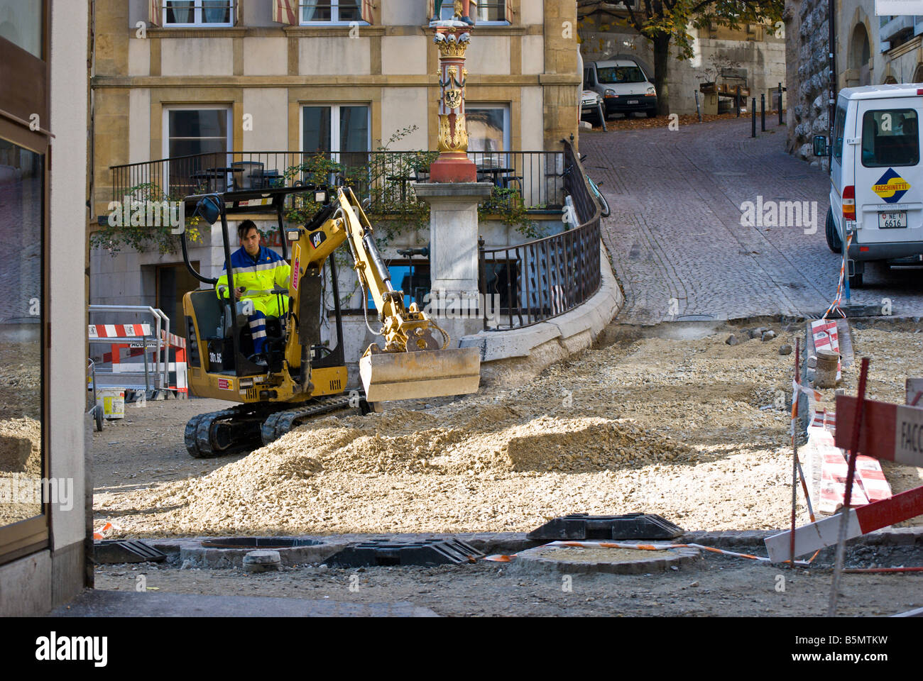 A construction worker operates a small back-hoe to flatten gravel in an ...