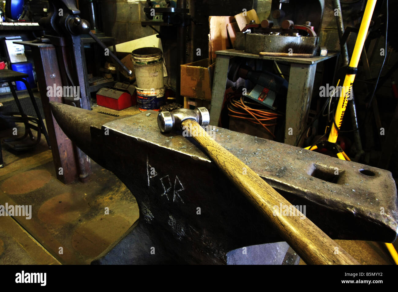 A hammer resting on an anvil with a blacksmith's tools behind Stock ...