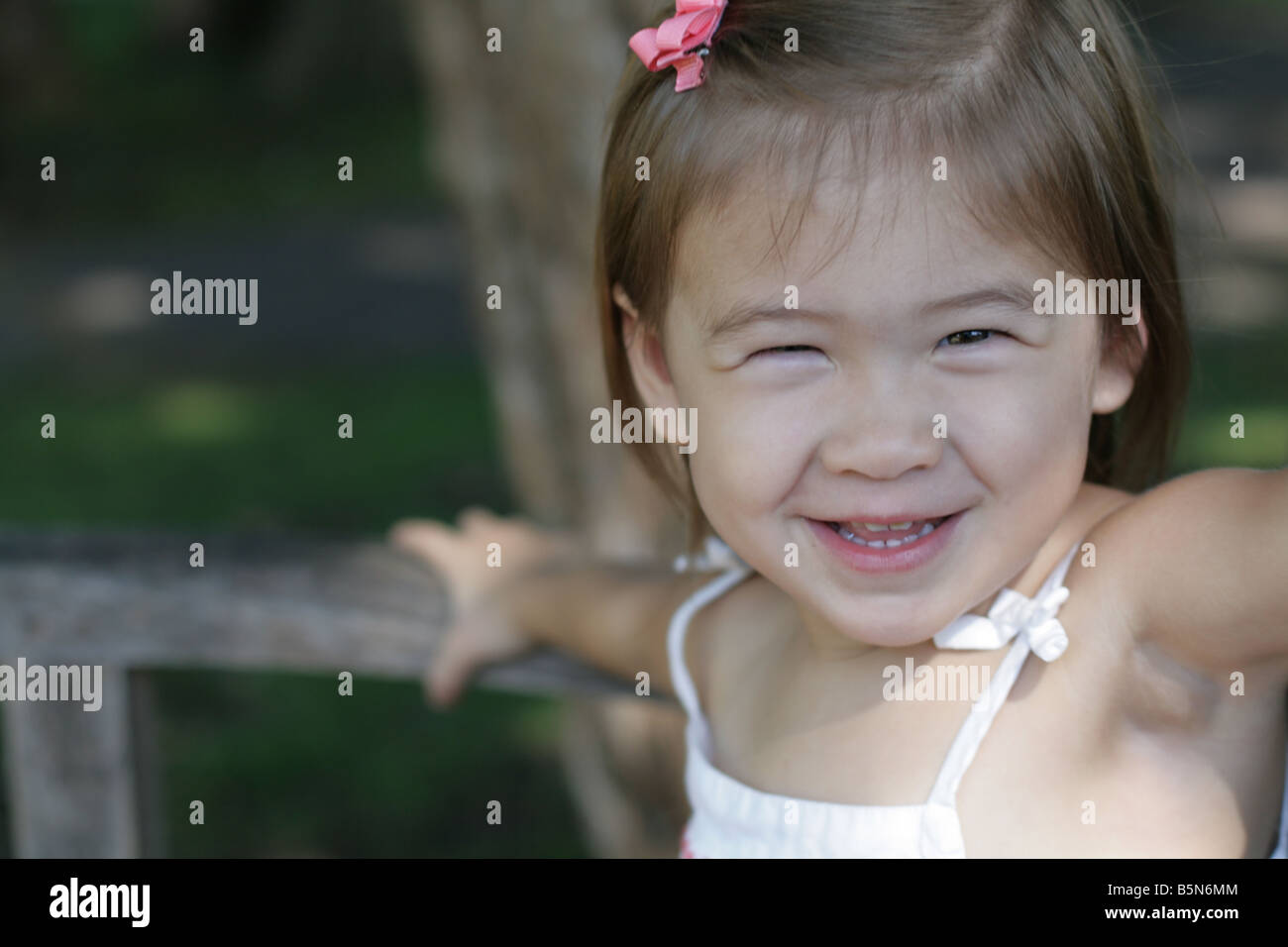 A 2-year-old girl smiles happily while sitting outside on a wooden ...